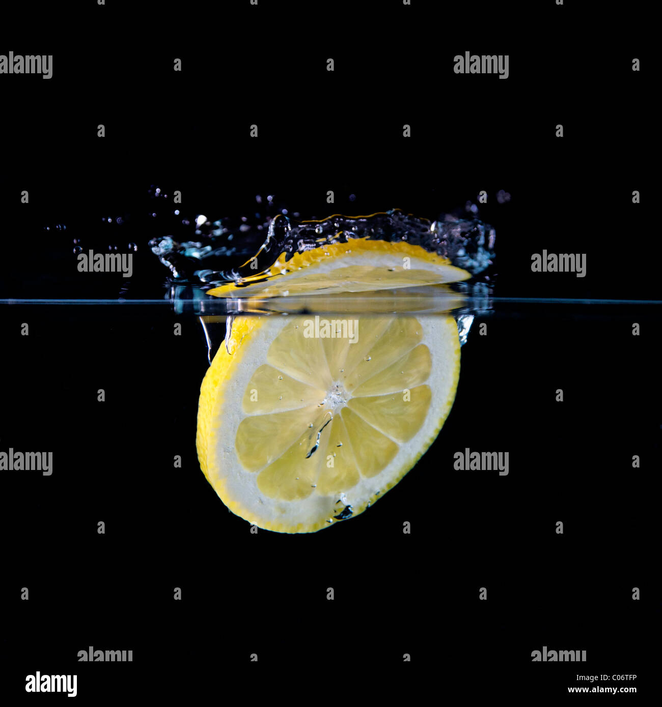 Slice of lemon dropped into water with a black background and a blue ...