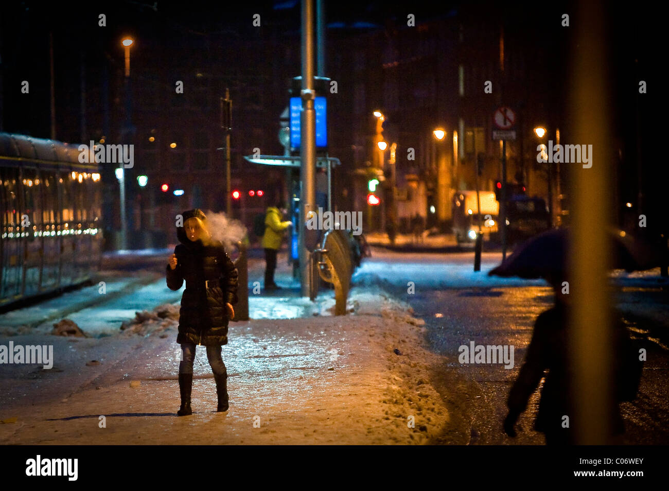 A woman smoking a cigarette tentatively walks across compacted snow and ...
