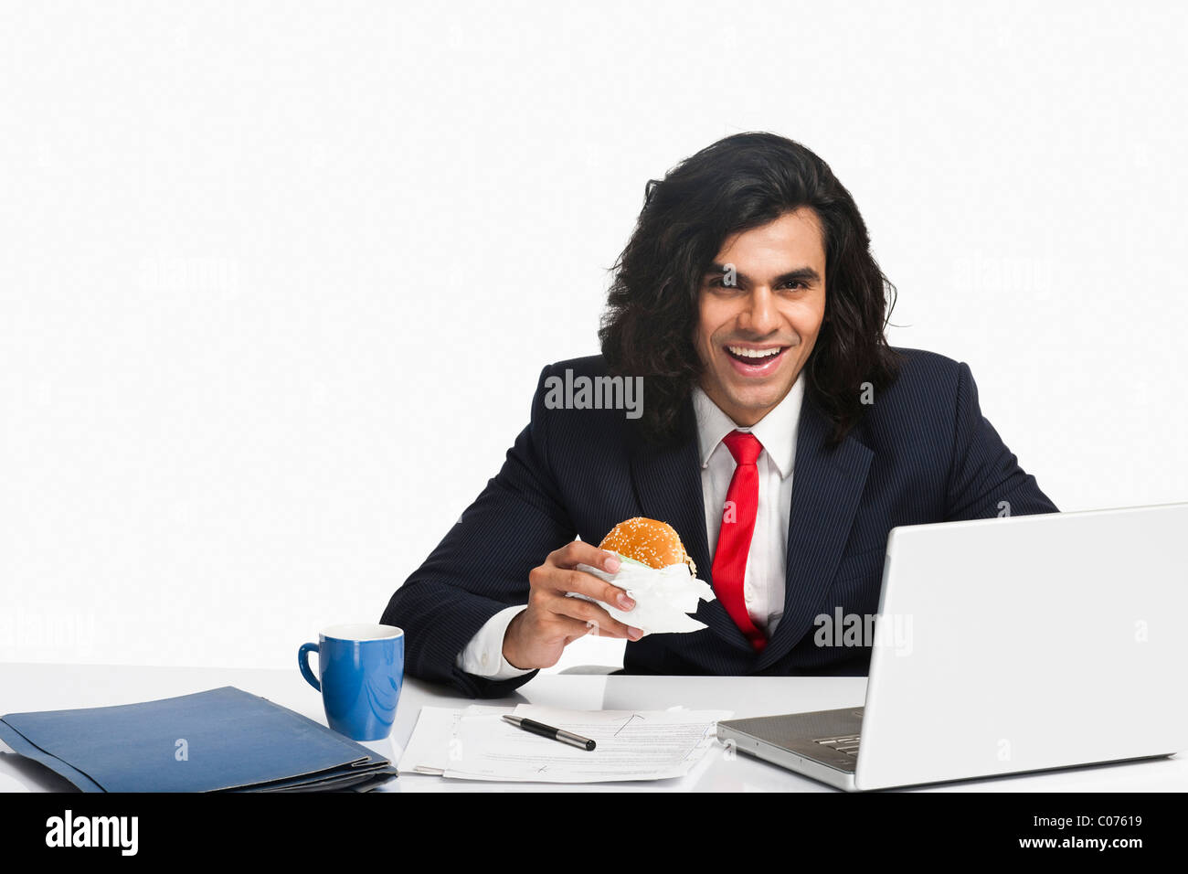 Businessman eating a burger at the desk Stock Photo - Alamy