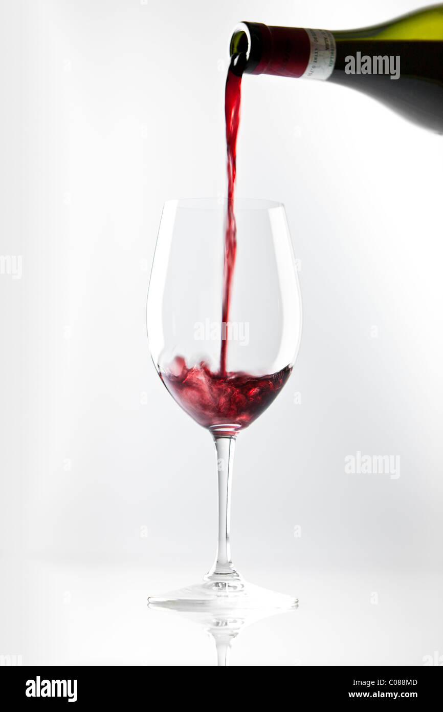 A glass of Red Wine being poured from the bottle on a white background ...