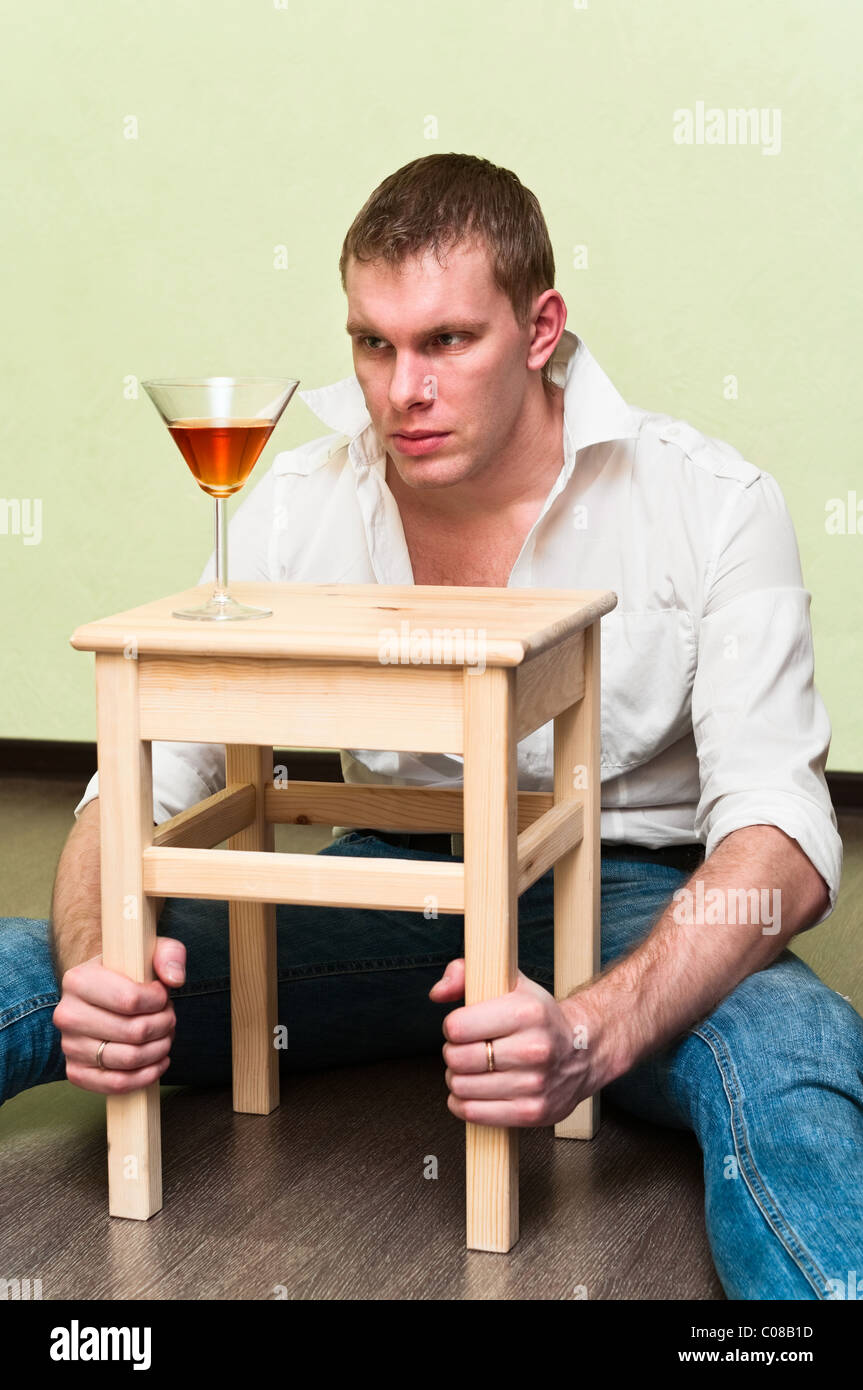 Drunken man sitting on floor with glass of alcohol and holding stool ...