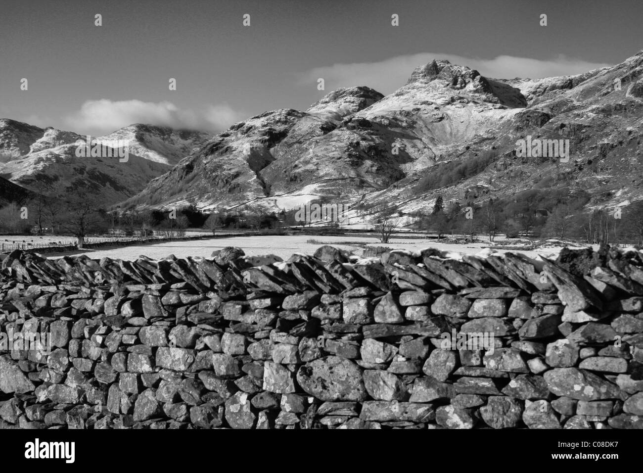 Dry stone wall on walkers path with snow on fields around Langdale ...