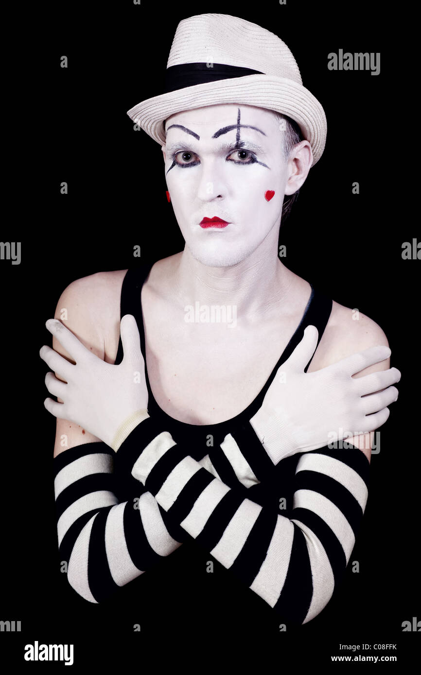 Studio portrait of serious theatrical clown in white hat and striped ...