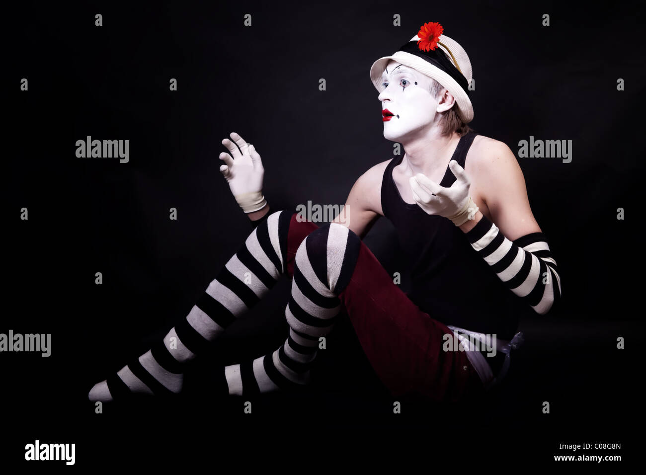 Studio portrait of Dramatic funny mime in white hat with red flower and ...