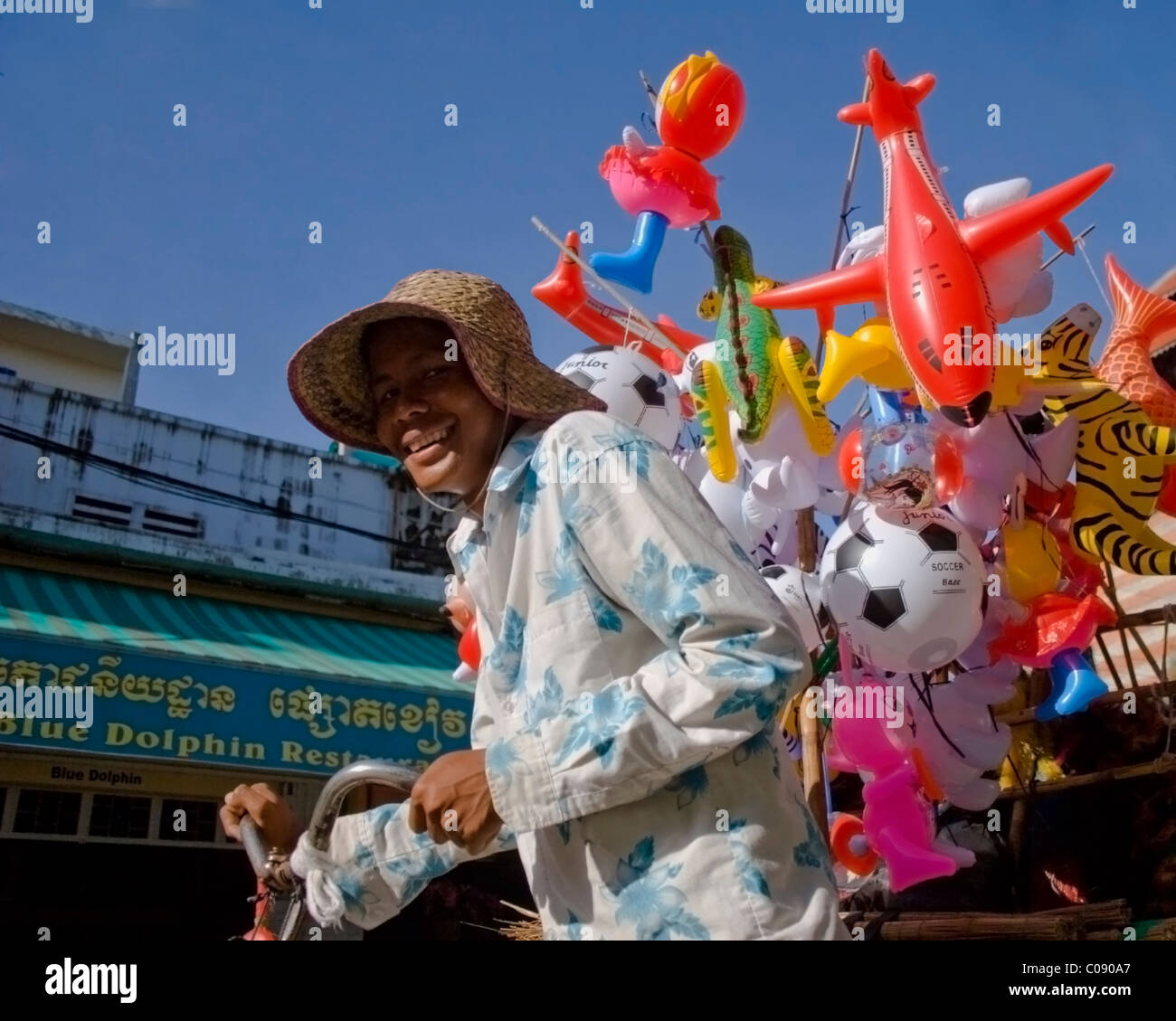 A toy balloon salesman wearing a straw hat is working on a city street ...