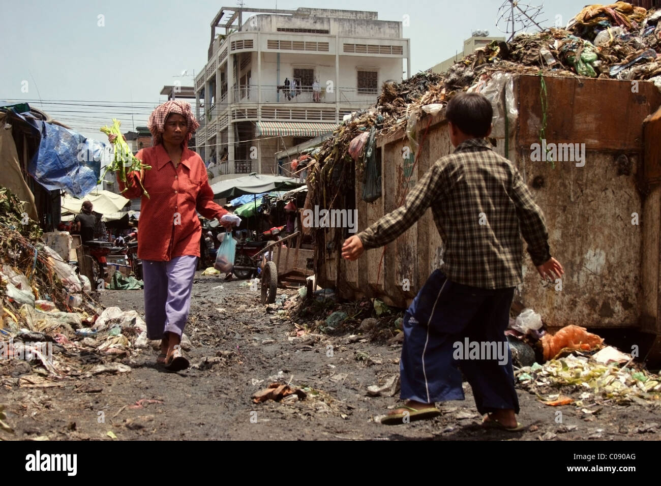 A boy and a woman are walking through an alley littered with rotting ...