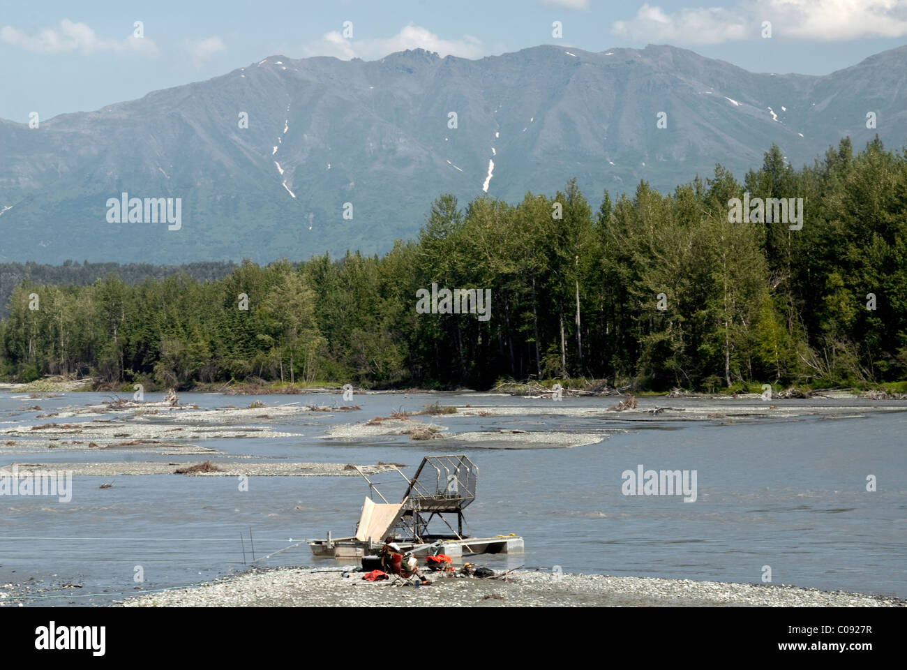 Two men relax on a gravel bar next to an aluminum fish wheel on the ...