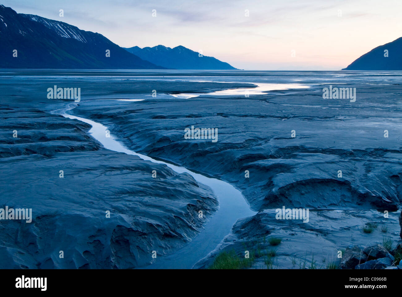 Evening sky reflects on a stream flowing through the mud flats of ...