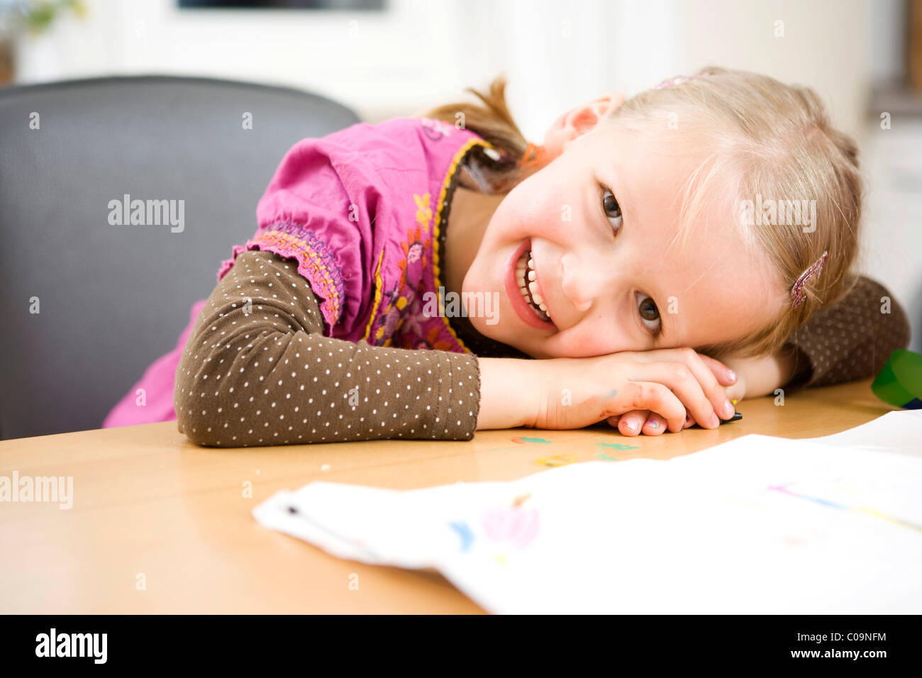 A girl smiling, head resting on her arms on the table Stock Photo - Alamy