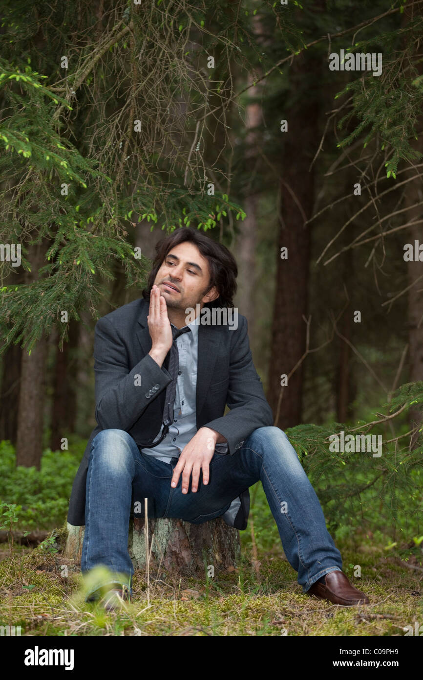 Young man sitting thoughtfully on a tree stump in a forest Stock Photo ...