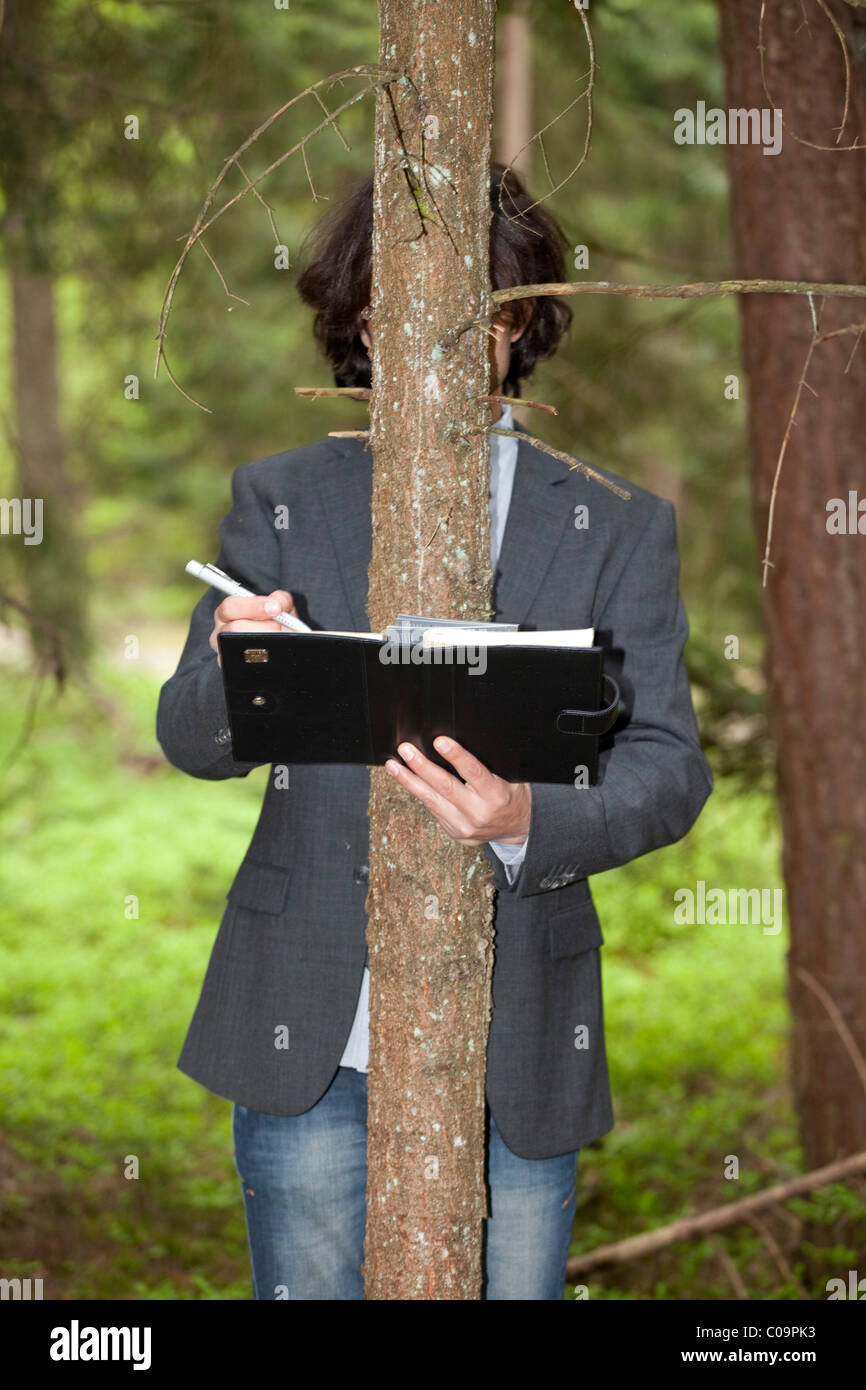 Businessman with diary behind a tree in a forest Stock Photo - Alamy