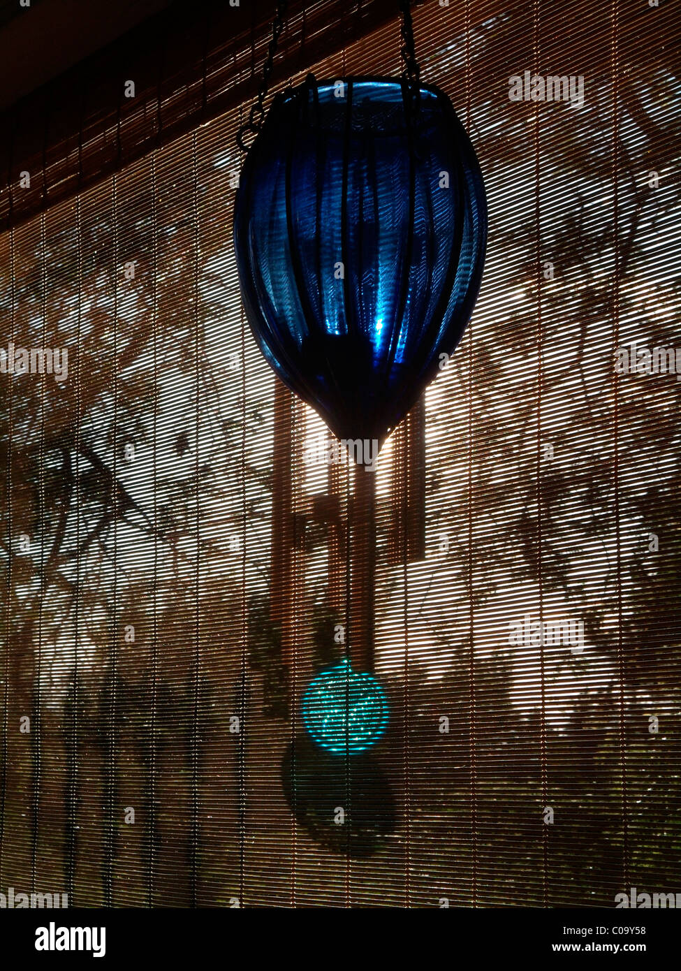 Blue glass planter and wind chimes hanging on a porch with bamboo ...