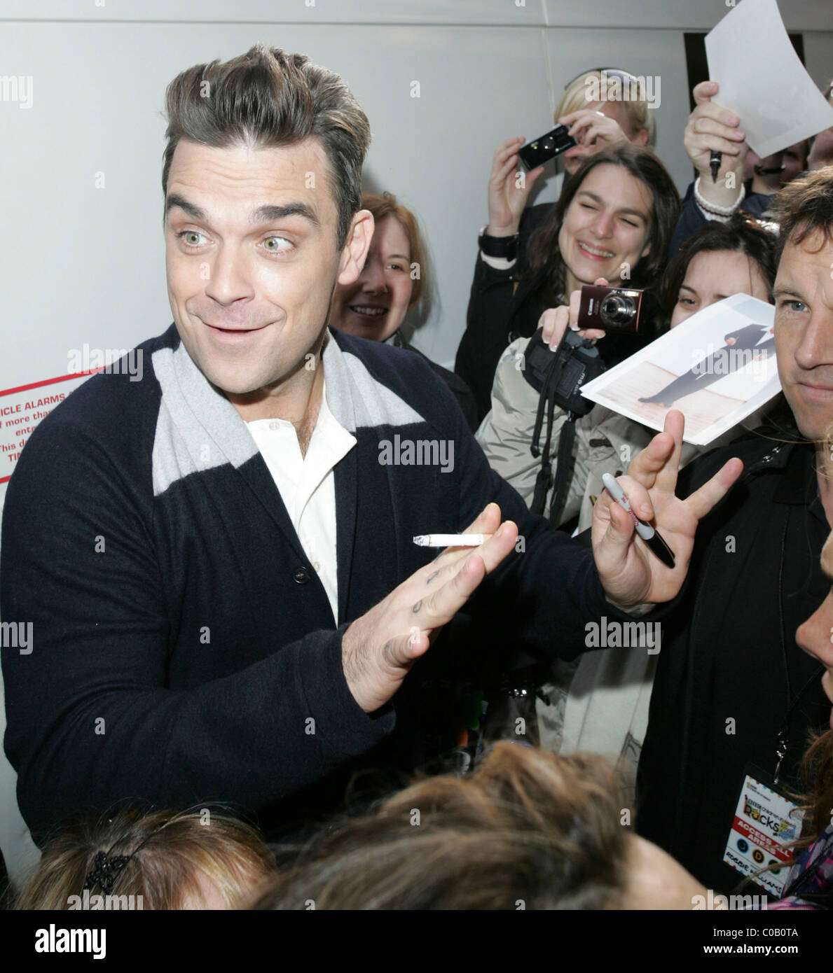 Robbie Williams signs autographs for fans while smoking a cigarette ...