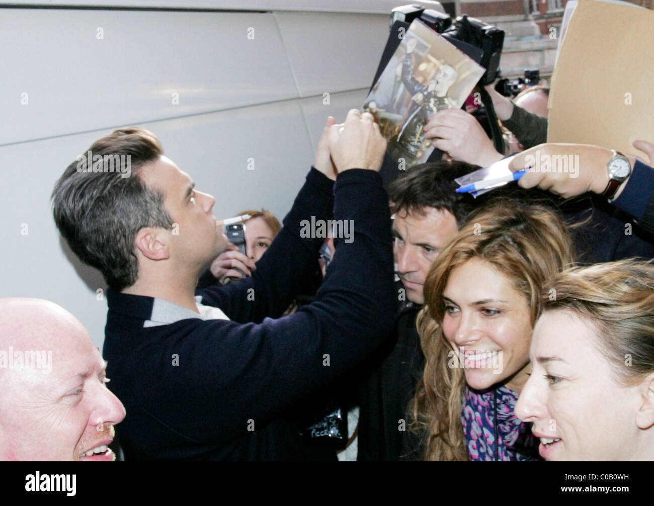 Robbie Williams signs autographs for fans while smoking a cigarette ...