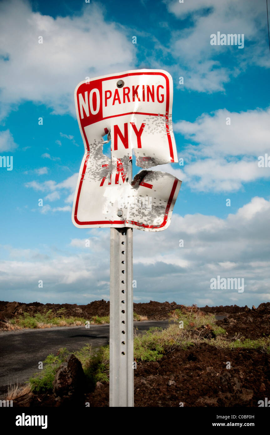 No Parking sign broken by bullets in front of an empty country road ...