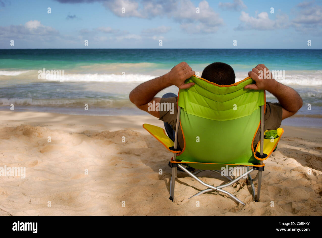 Man in chair relaxing on beach. Person sitting in green collapsible ...