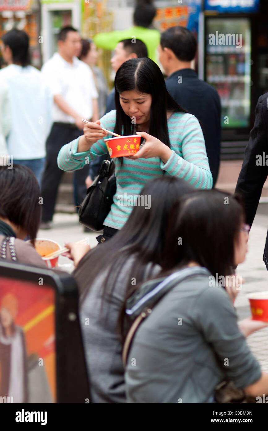 Chinese woman eating on a street with chopsticks Stock Photo - Alamy