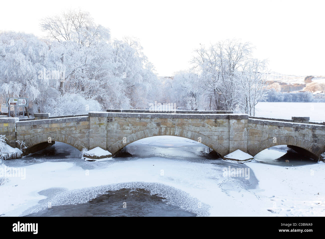 Sandstone bridge over the frozen and snow covered River Calder ...