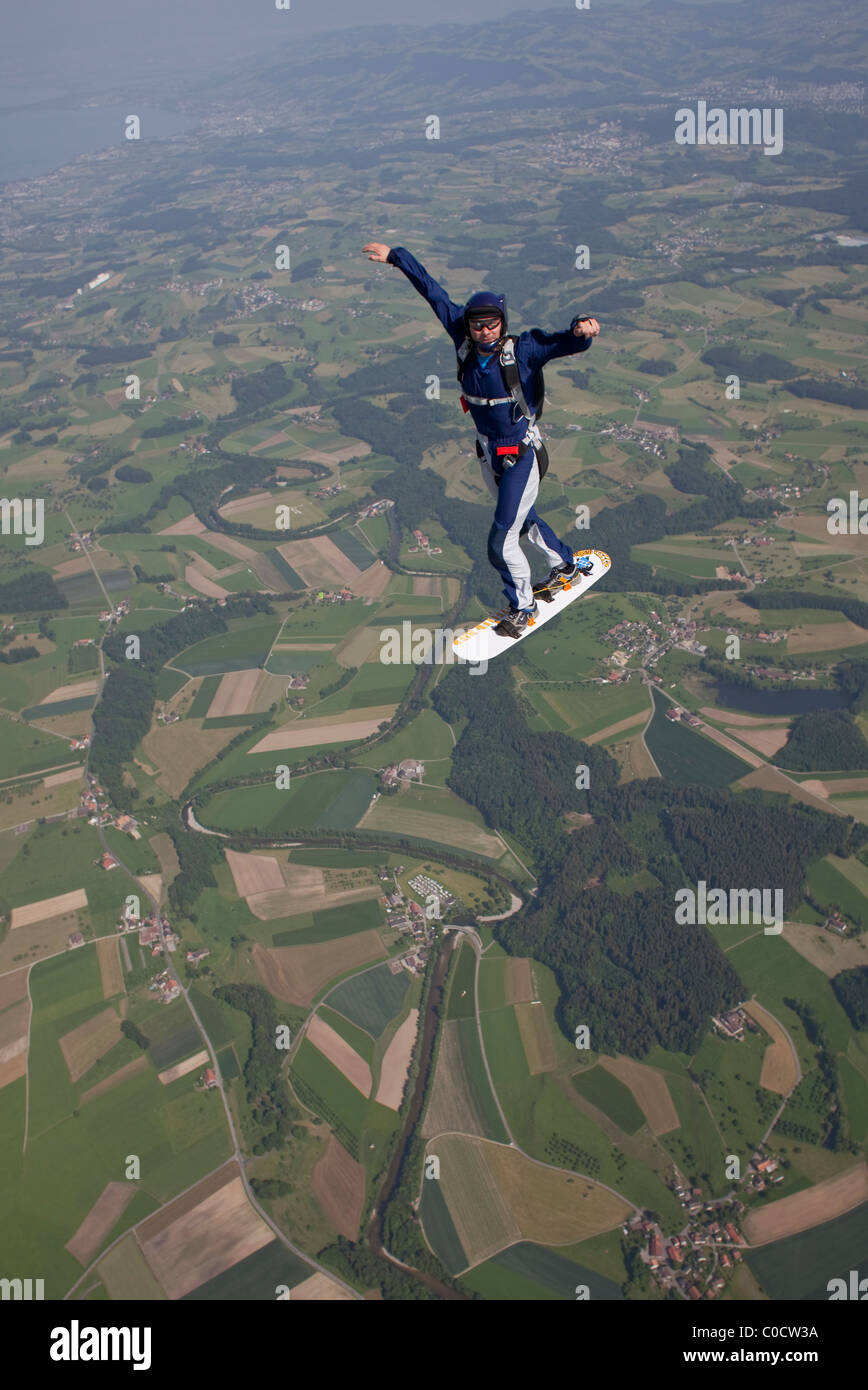 Skydiver is surfing on his sky board over a green field area and having ...