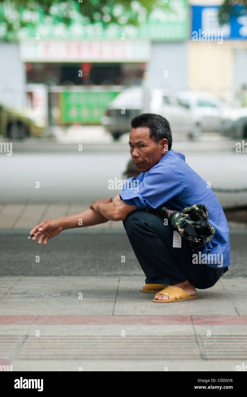 Chinese man with a cigarette in his hands crouching in the middle of a ...