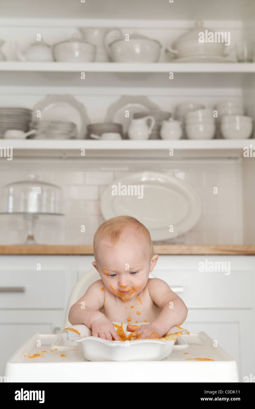 Messy baby eating in high chair Stock Photo - Alamy