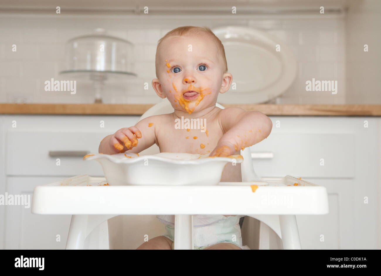 Messy baby eating in high chair Stock Photo - Alamy