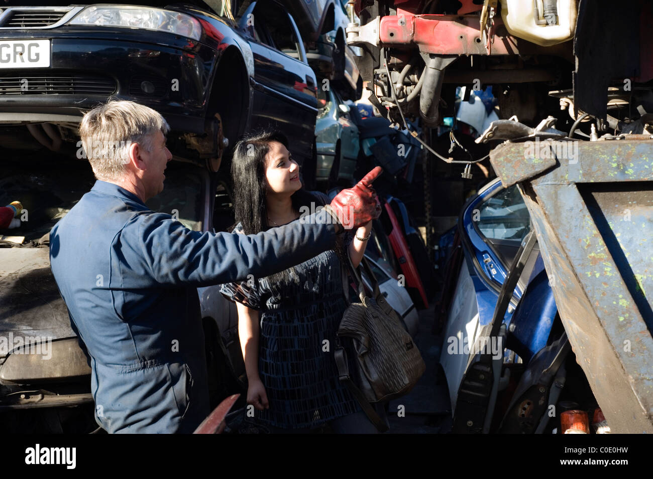 scrapyard worker showing young woman spare part on scrap car Stock ...
