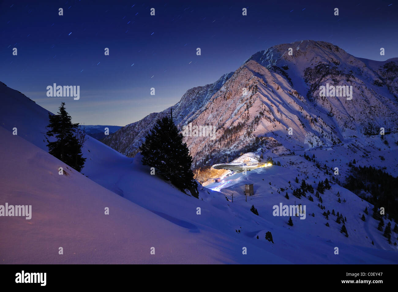 Moonlit mountain scene with snow, trees and star trails in the sky ...
