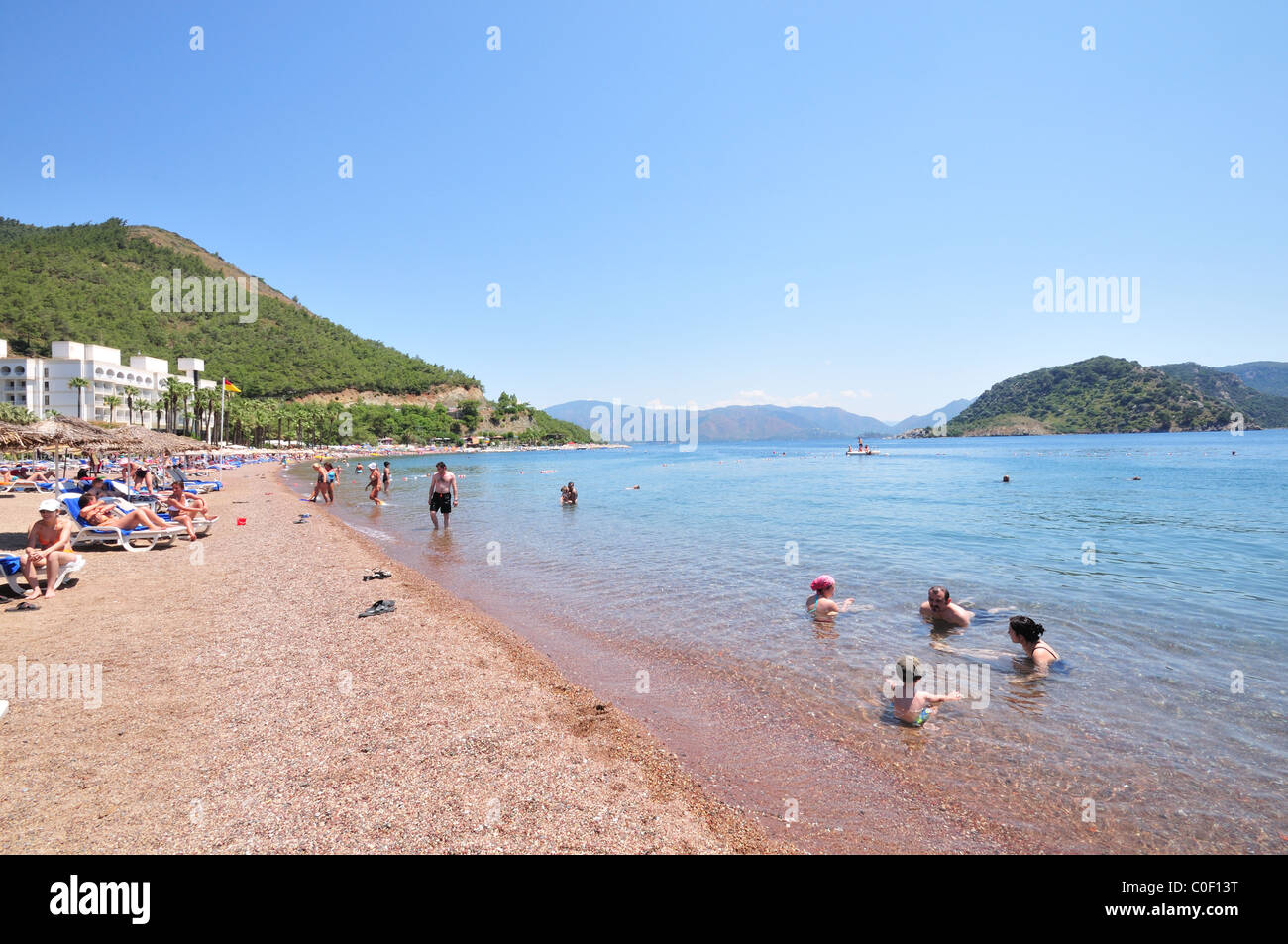 View of a sandy beach with people sunbathing and swimming in the Aegean ...