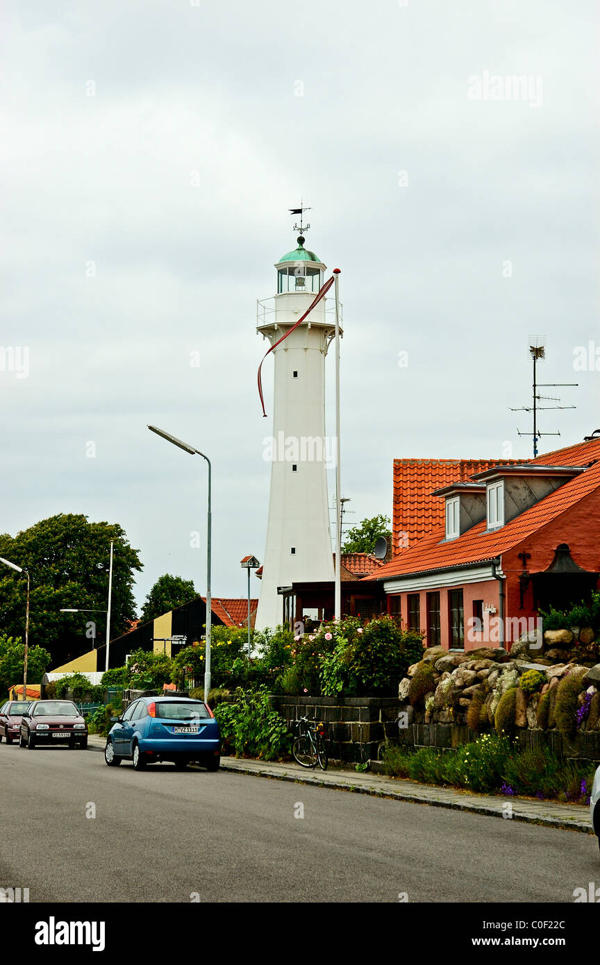 A tall white lighthouse stands between modern houses with blooming ...