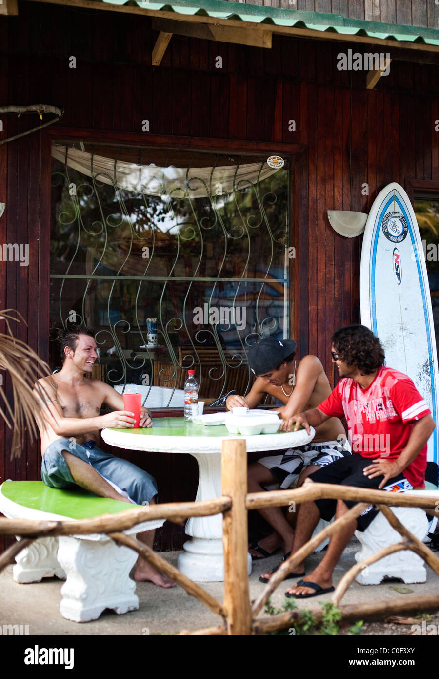 Three surfers sit outside a restaurant talking and eating takeout Stock ...