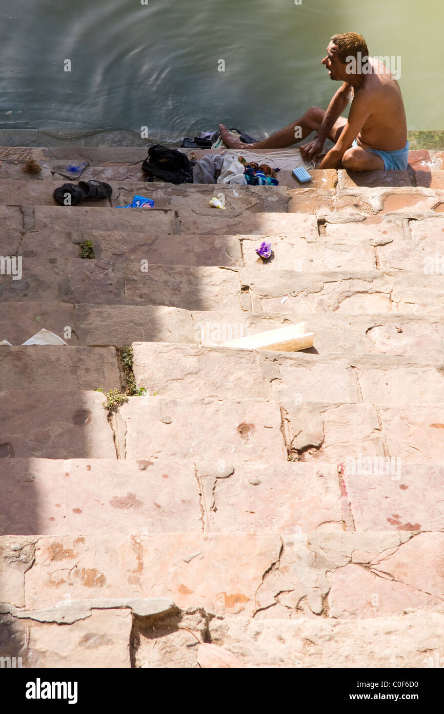 Indian man washing clothes by sitting on the stairs of the water tank ...