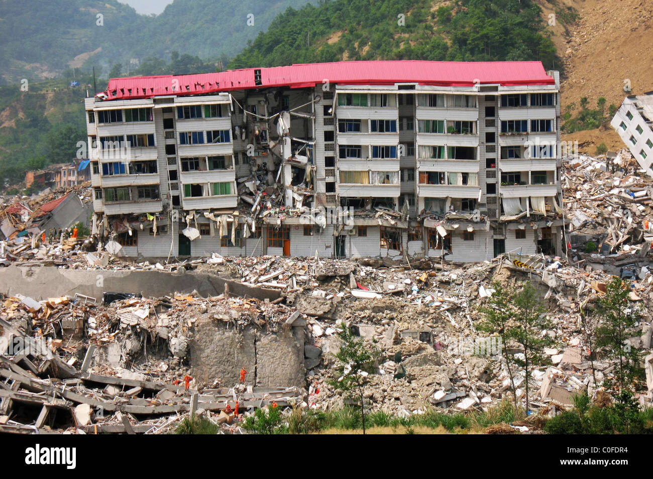 Rescue workers can be seen in their red outfits among the rubble as ...