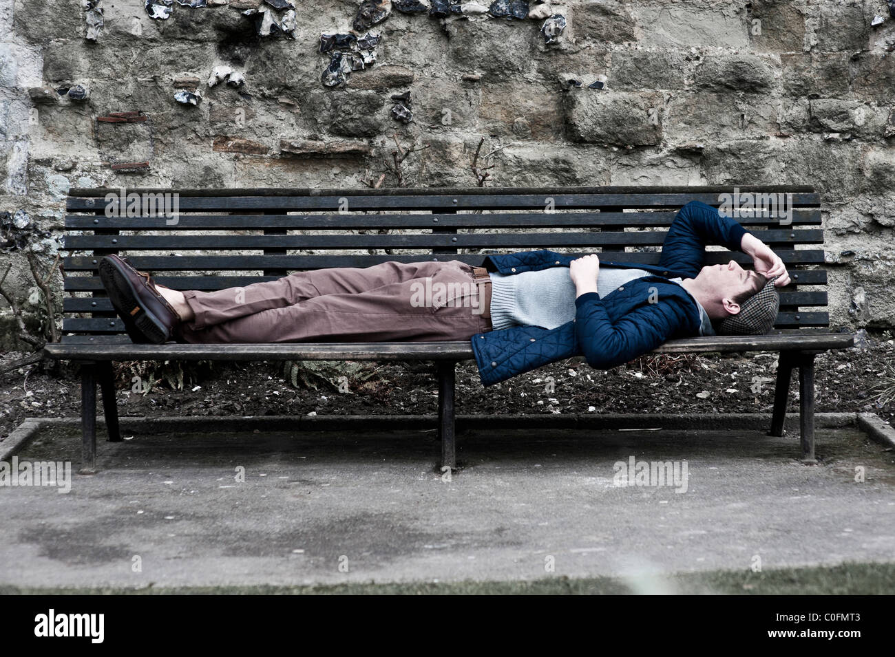 Young man, lying on bench in public place, asleep Stock Photo - Alamy