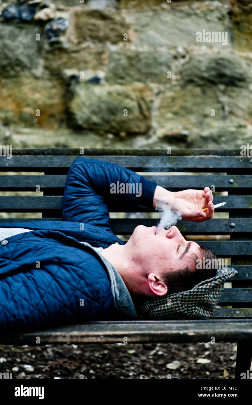 Young man laying on bench blowing out cigarette smoke Stock Photo - Alamy