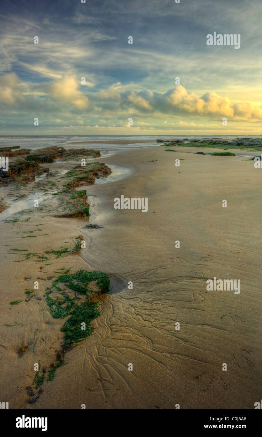 Beautiful sunrise landscape over sandy beach with rock and cliff detail ...