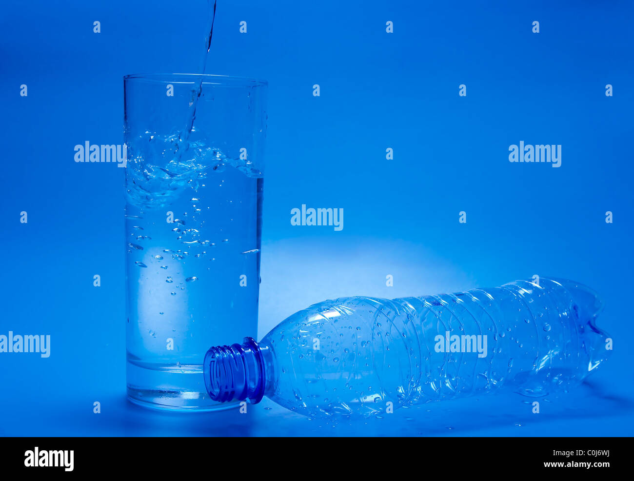 Water pouring into a glass, empty bottle next to it Stock Photo - Alamy