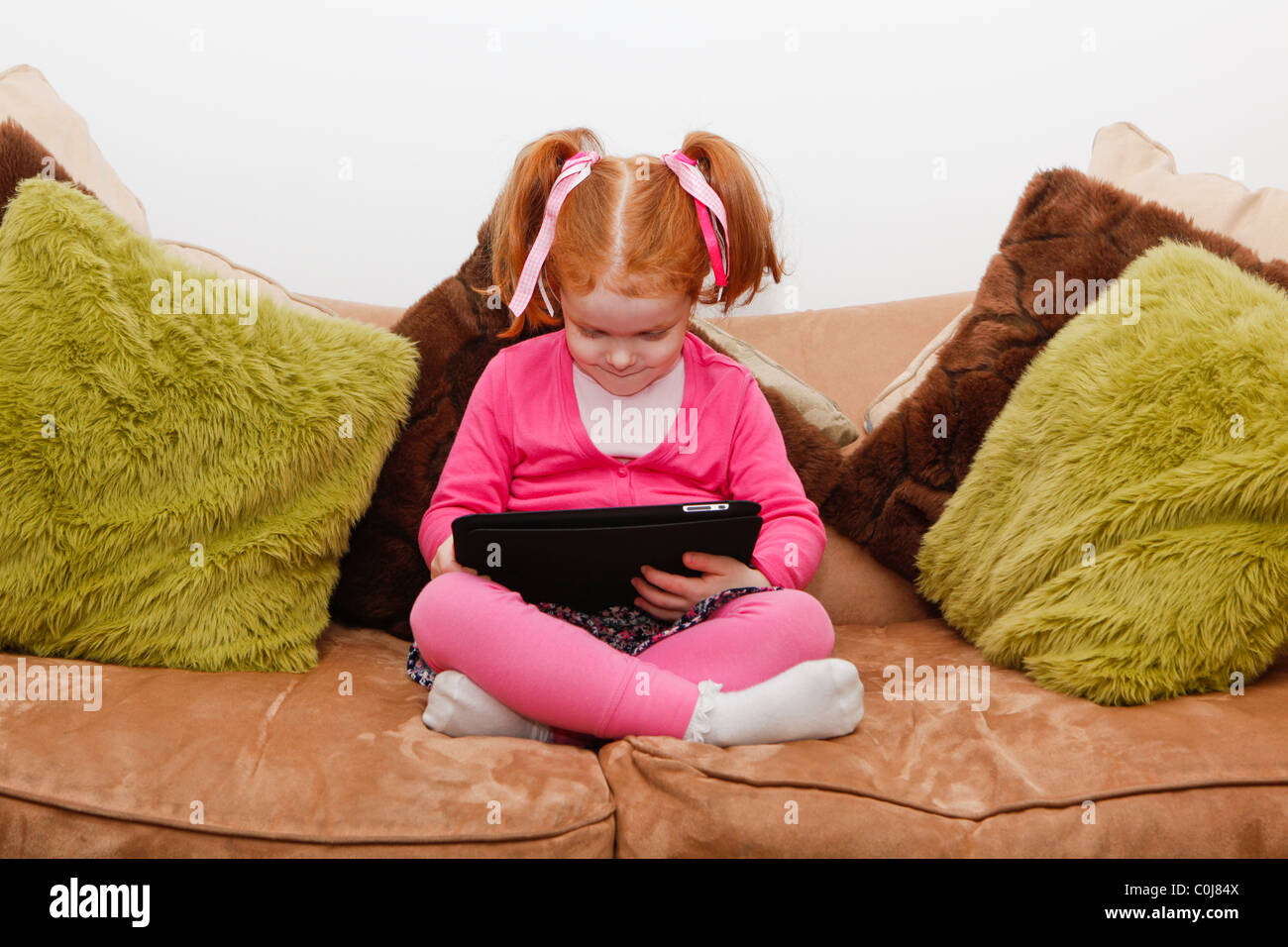Little girl with red hair playing on the Ipad, computer tablet, whilst ...