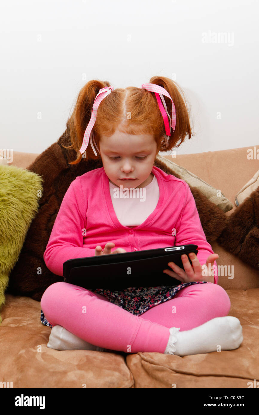 Little girl with red hair playing on the Ipad, computer tablet, whilst ...
