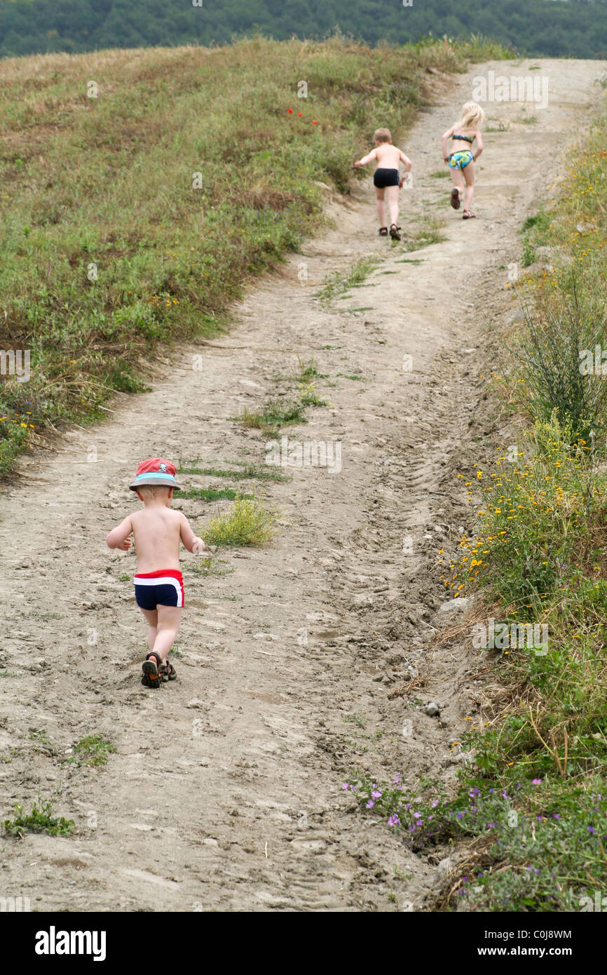 A young boy trying to chase after two older children running up a hill ...