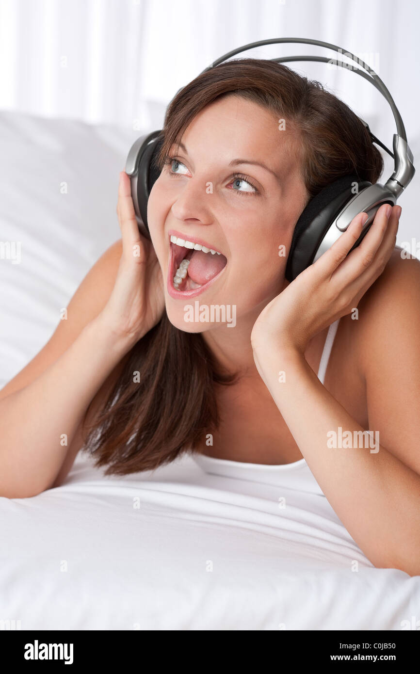 Young woman with headphones singing on white sofa Stock Photo - Alamy