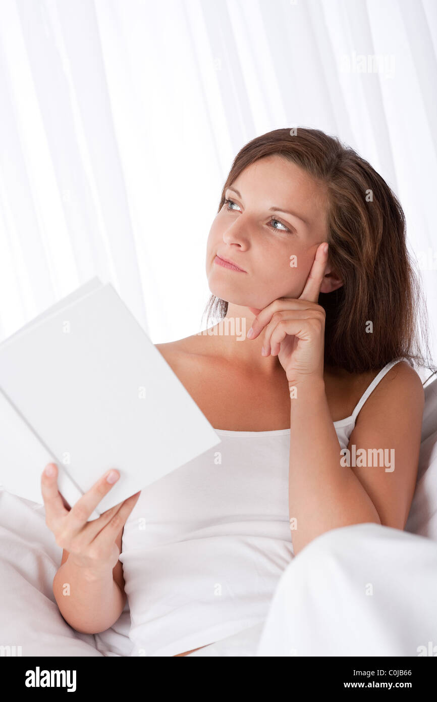 Woman thinking while reading book on sofa Stock Photo - Alamy