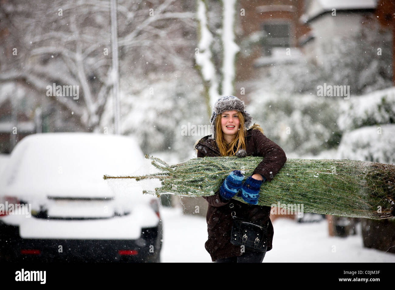A young woman carrying a Christmas tree along a snowy street Stock ...