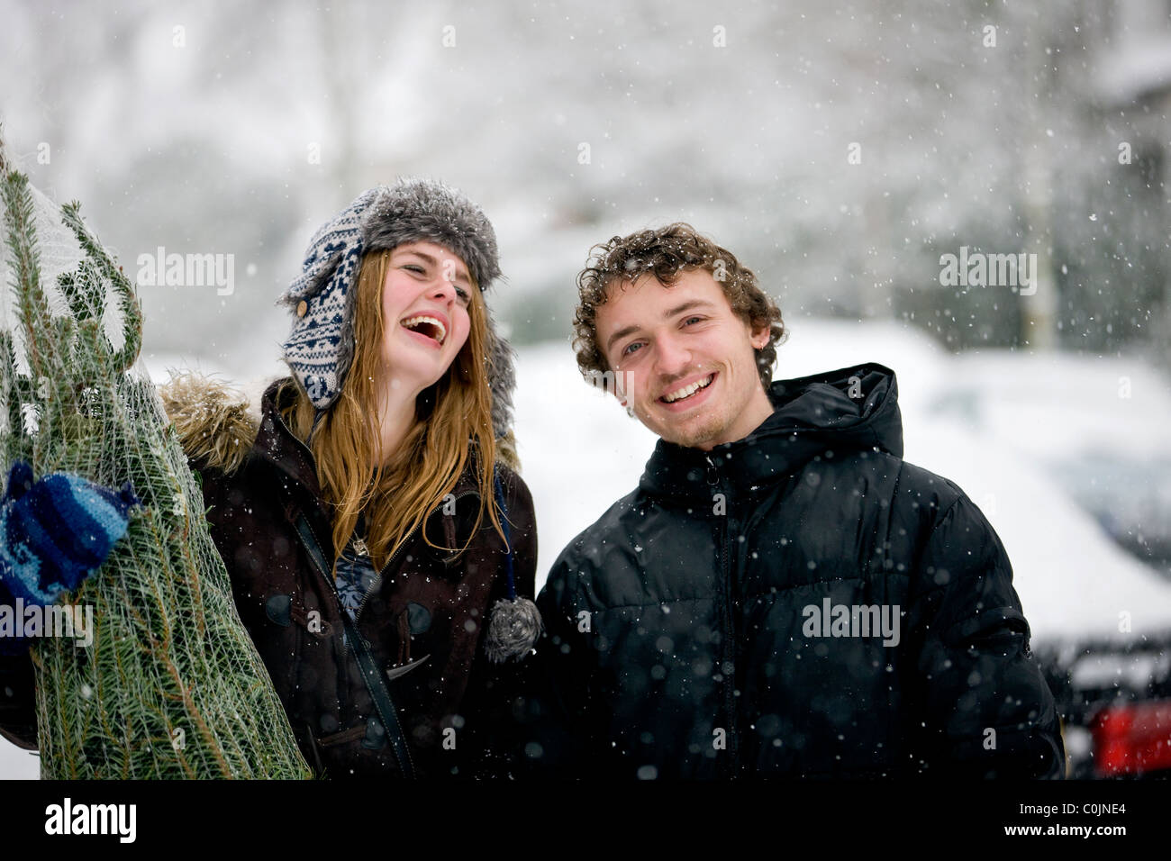 A young couple with a Christmas tree in the snow, laughing Stock Photo ...