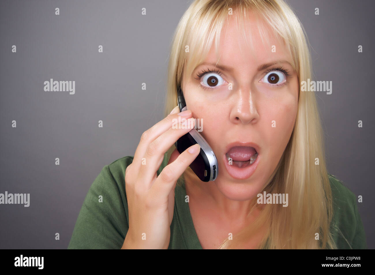 Stunned Blond Woman Using Cell Phone Against a Grey Background Stock ...