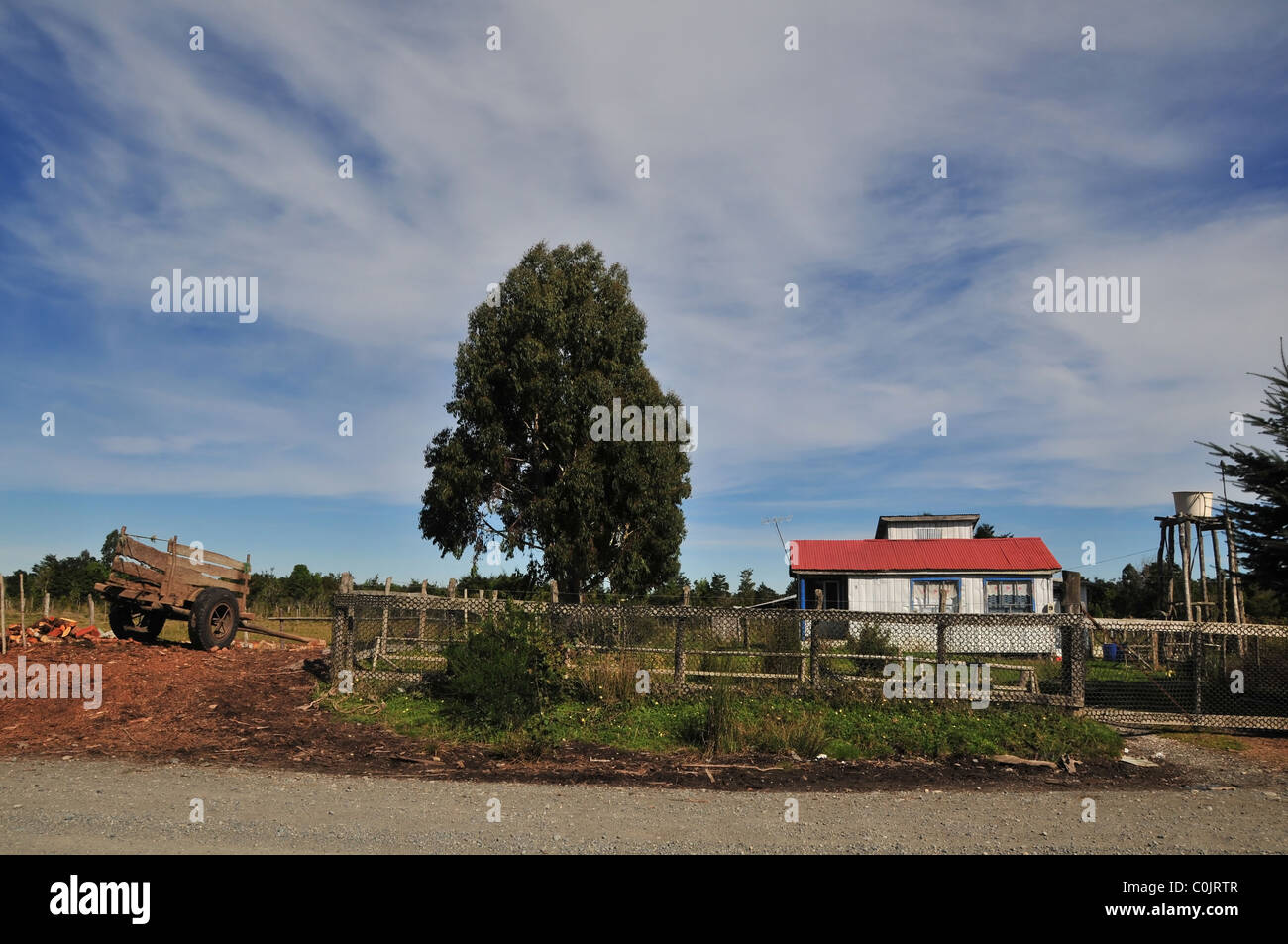 Roadside rural view of red farmhouse with log cart and plastic bucket ...