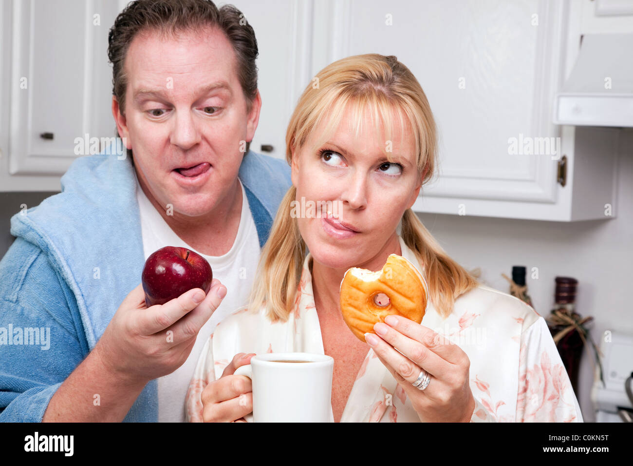 Competitive Couple in Kitchen Eating Donut and Coffee or Healthy Fruit ...