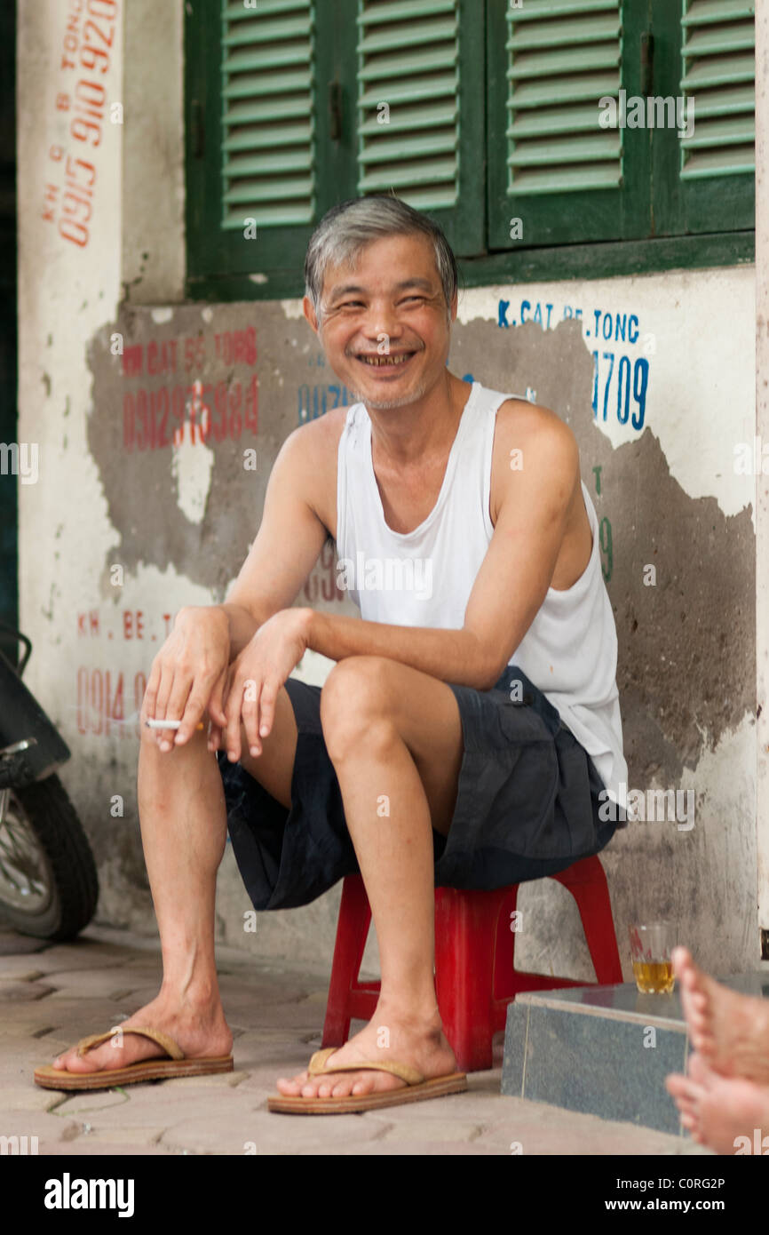Vietnamese man sitting on a red plastic chair, with a cigarette in his ...