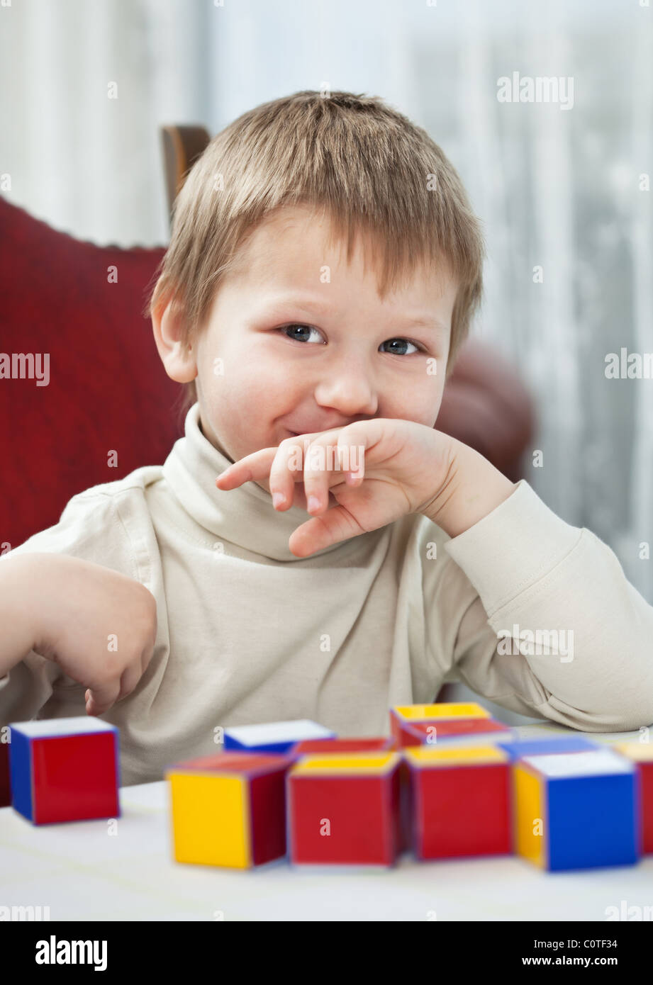 Smiling blond boy seating at the table with colorful blocks Stock Photo ...