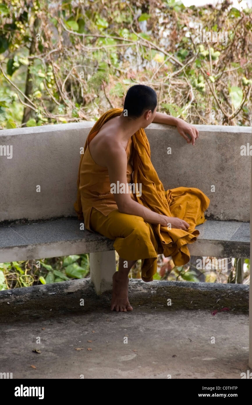 A Buddhist monk is sitting alone on a bench at a beautiful Buddhist ...